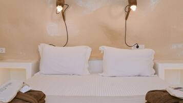 Quarto de hotel com duas camas, roupa de cama branca e duas luminárias na parede.