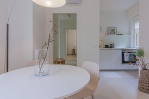 Cozinha moderna com armários brancos, área de jantar com mesa redonda e um vaso com galhos.