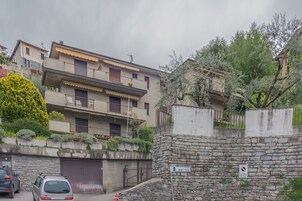 Um edifício residencial com vários andares, varandas, uma parede de pedra e uma área de estacionamento.