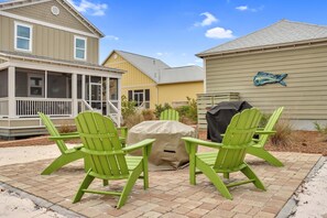 Um pátio com cadeiras Adirondack verdes, uma churrasqueira coberta e uma casa com um mural de peixes.