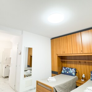 Quarto de hotel com cama, guarda-roupa de madeira, mesa de cabeceira e espelho.