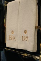 Duas toalhas brancas com a inscrição 'BRA' bordada, penduradas num suporte de toalhas de metal preto.