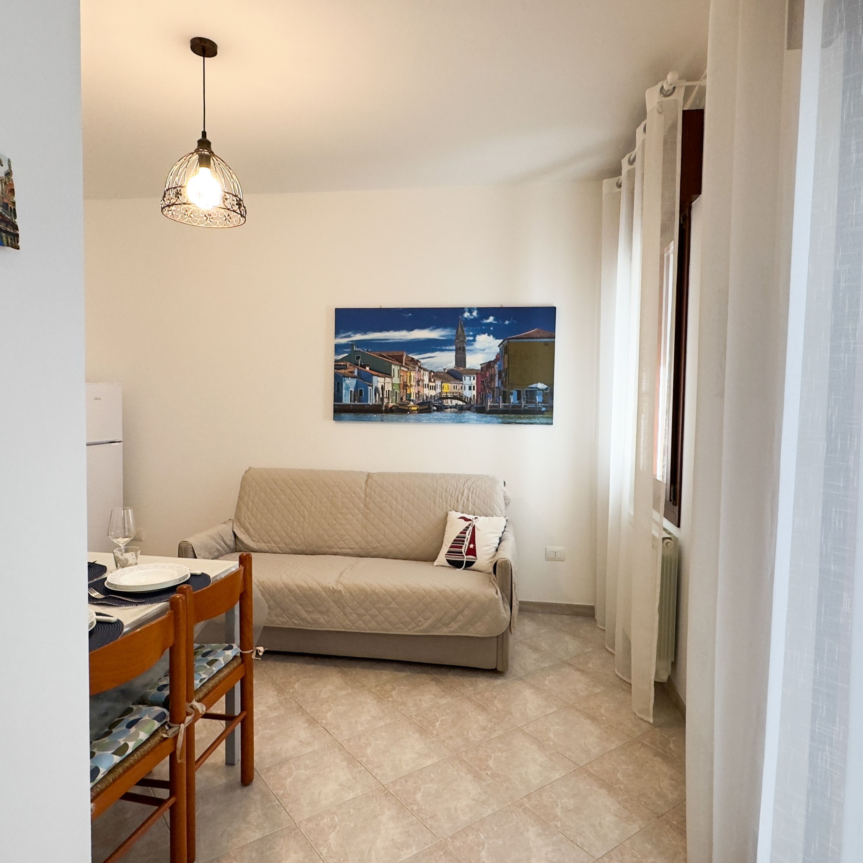 Um quarto pequeno e acolhedor com uma mesa de jantar, um sofá e uma pintura de uma paisagem urbana.