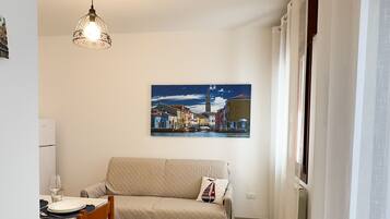 Um quarto pequeno e acolhedor com uma mesa de jantar, um sofá e uma pintura de uma paisagem urbana.