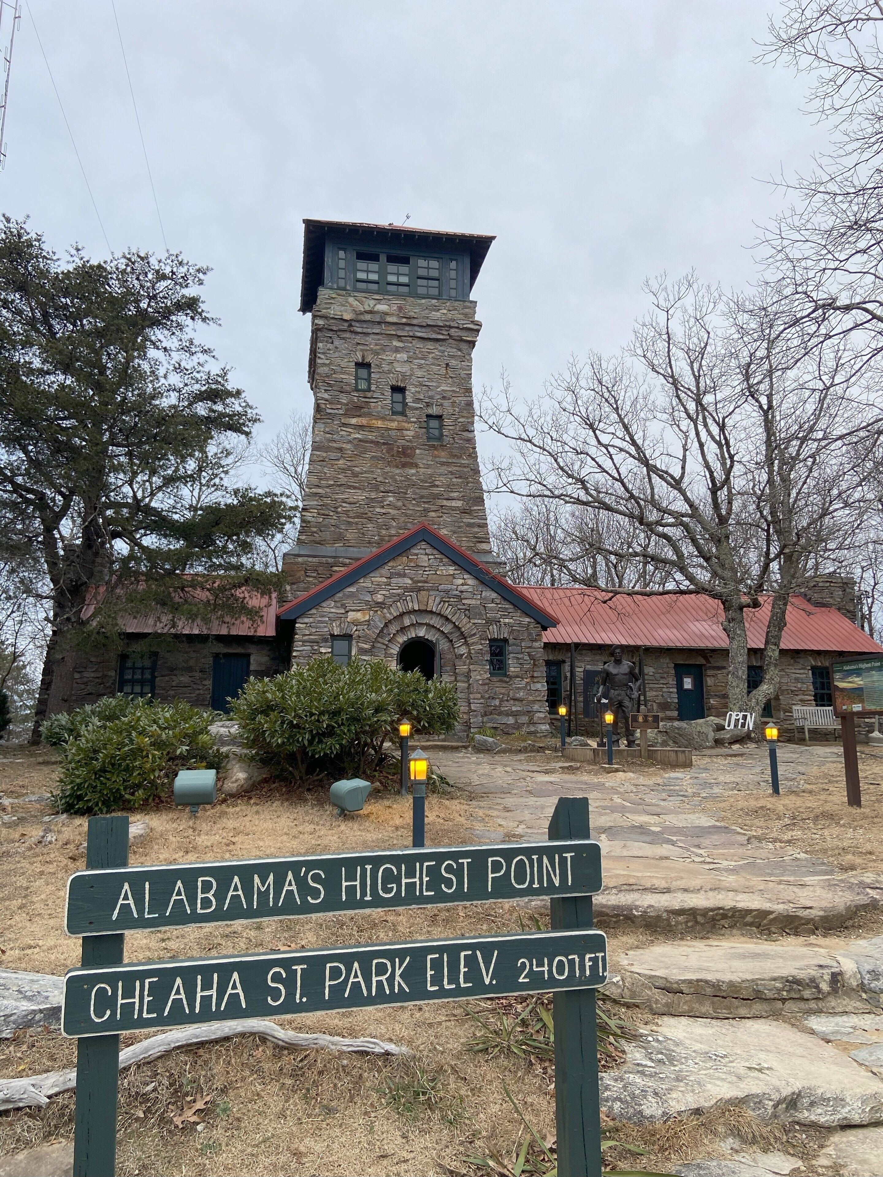 Uma torre de pedra com telhado vermelho, cercada por árvores e uma placa indicando ser o ponto mais alto do Alabama, a 732 metros.