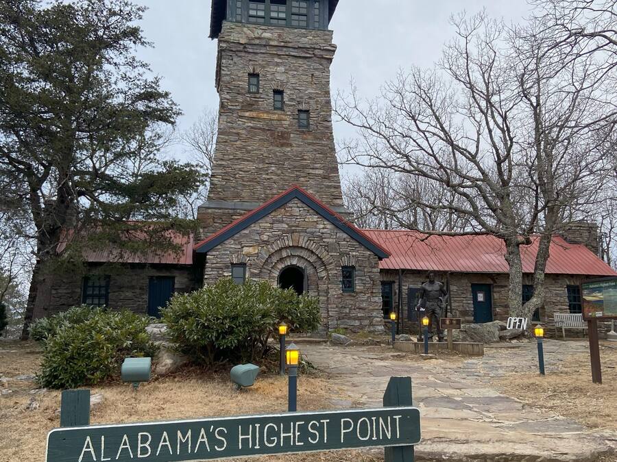 Uma torre de pedra com telhado vermelho, cercada por árvores e uma placa indicando ser o ponto mais alto do Alabama, a 732 metros.