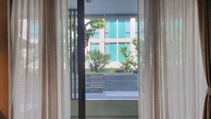 Quarto com vista para um edifício e uma pequena área externa com espaço para sentar.
