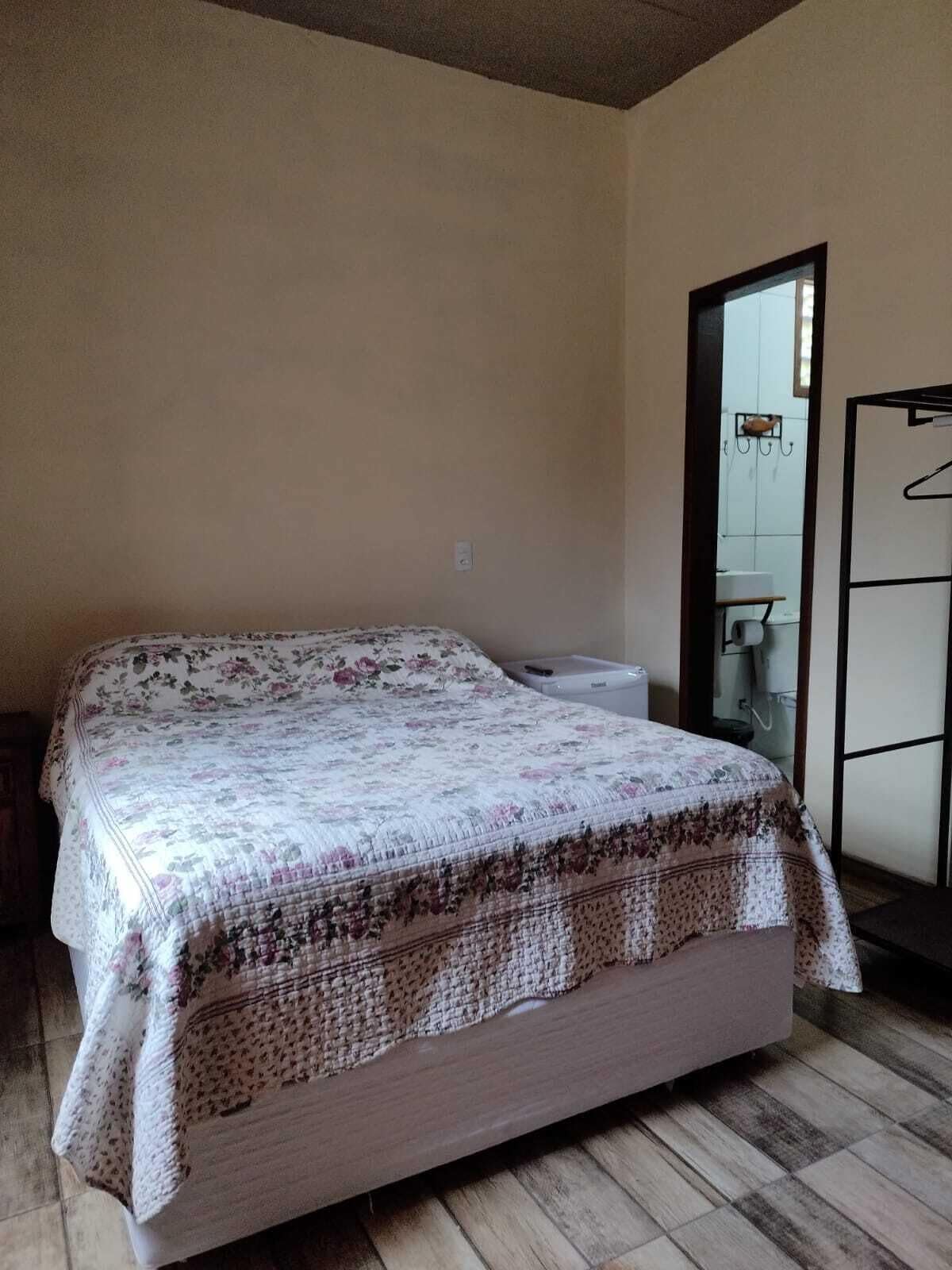 Quarto com cama, guarda-roupa e banheiro visível por uma porta aberta.