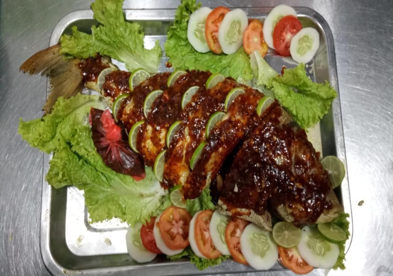 Uma bandeja de asas de frango grelhadas com um molho escuro, decorada com alface, tomates fatiados e gomos de limão.