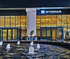 Um hotel Wyndham com fachada de vidro ampla, uma coluna central e um recurso de água em primeiro plano.