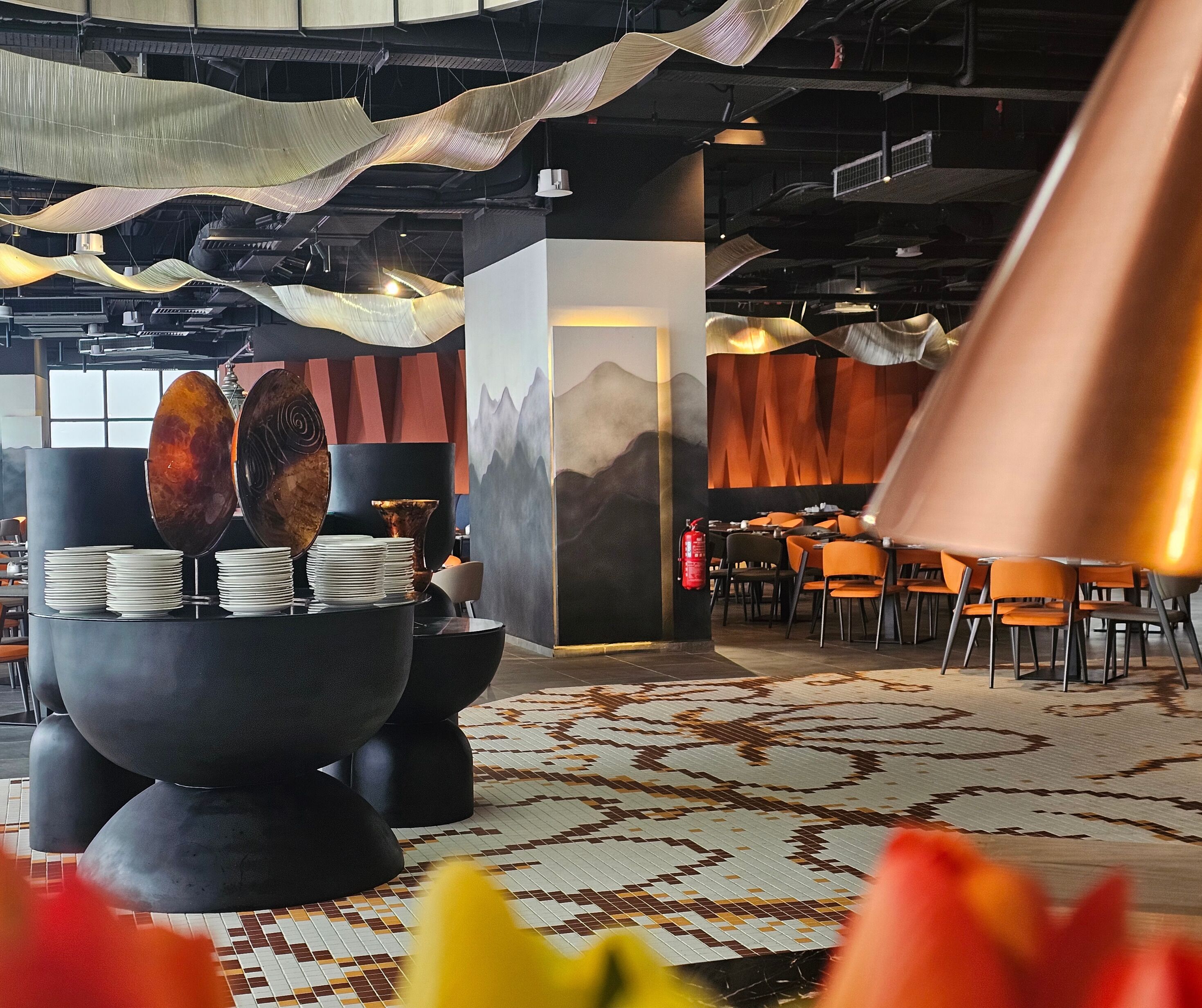 Interior de restaurante moderno com tetos altos, arte abstrata nas paredes e piso estampado.