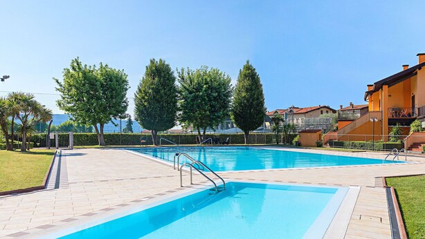 Piscina com deck revestido, rodeada por árvores e edifícios residenciais.