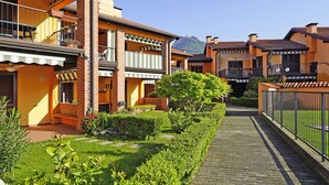 Um pátio com um caminho pavimentado, rodeado por edifícios com varandas e uma montanha ao fundo.