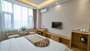 Quarto de hotel com uma cama grande, uma TV, uma escrivaninha, uma cadeira e uma pequena mesa com uma planta.