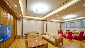 Uma sala de estar ampla, com piso de madeira, uma grande TV de tela plana, um sofá, uma mesa de centro e um espaço de jantar com cadeiras vermelhas e uma mesa posta para refeição.