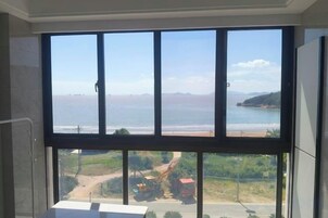 Quarto com uma grande janela que dá para uma praia e um canteiro de obras.