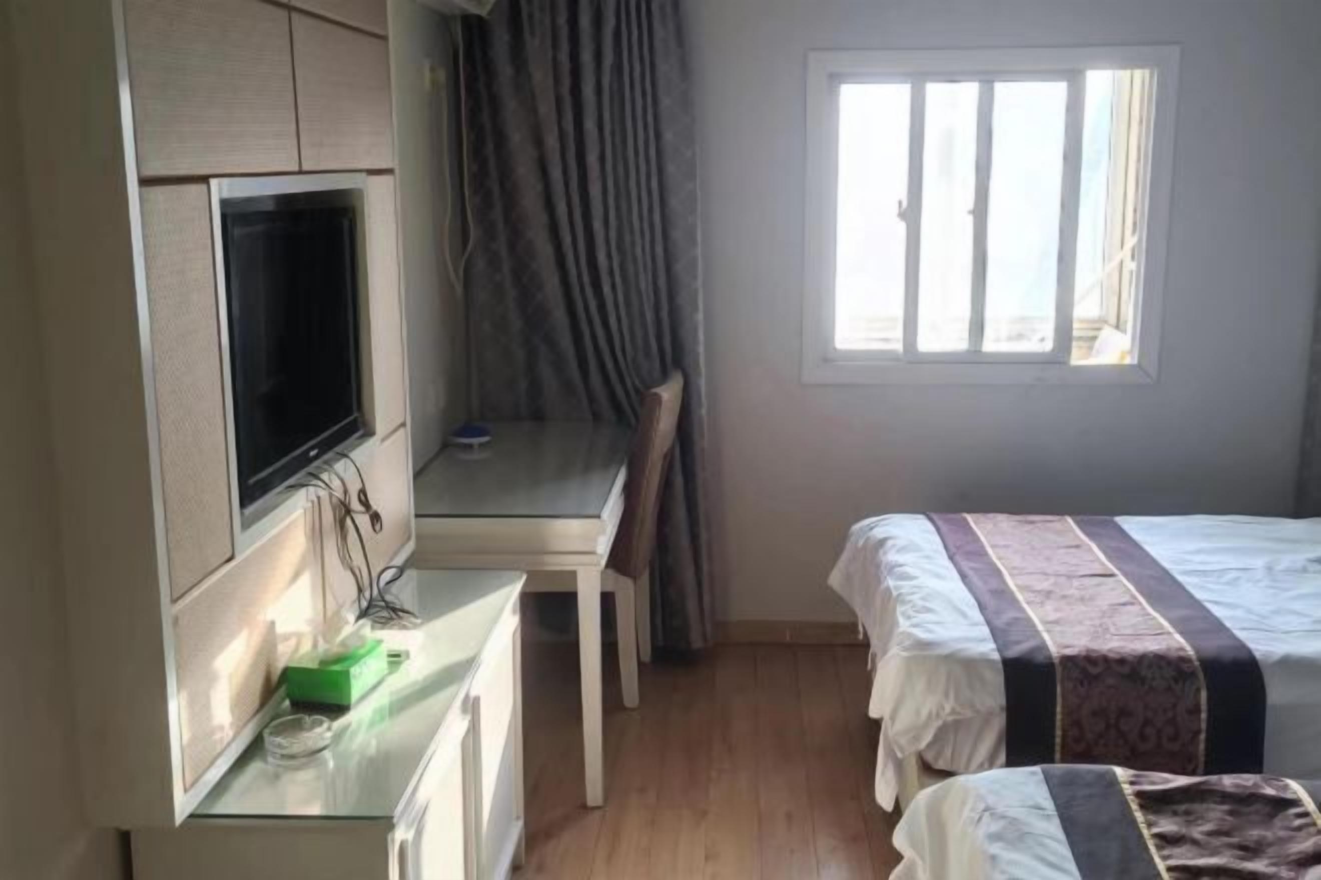 Quarto com escrivaninha, televisão, duas camas, janela e cortina.