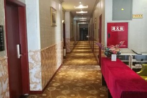 Corredor de hotel com carpete estampado, mesa com carpete vermelho e placa de segurança contra incêndio.