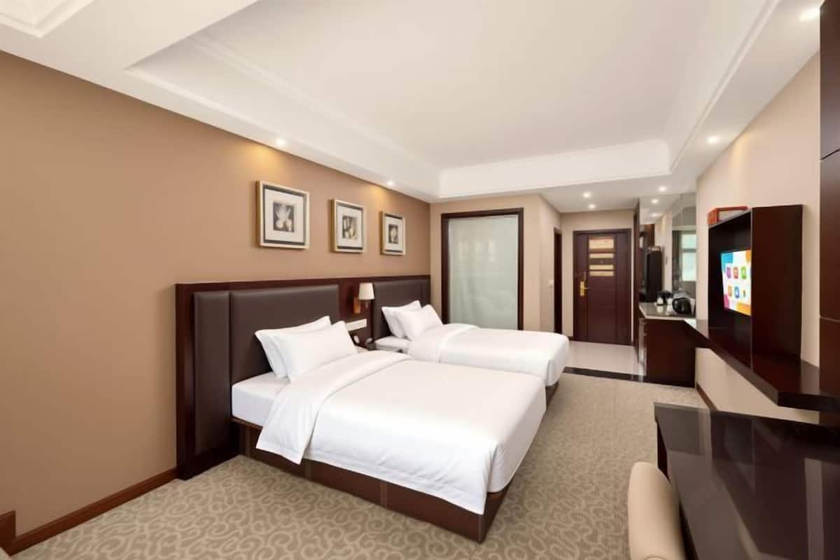 Quarto de hotel com duas camas, televisão, escrivaninha e banheiro visível através de uma porta.