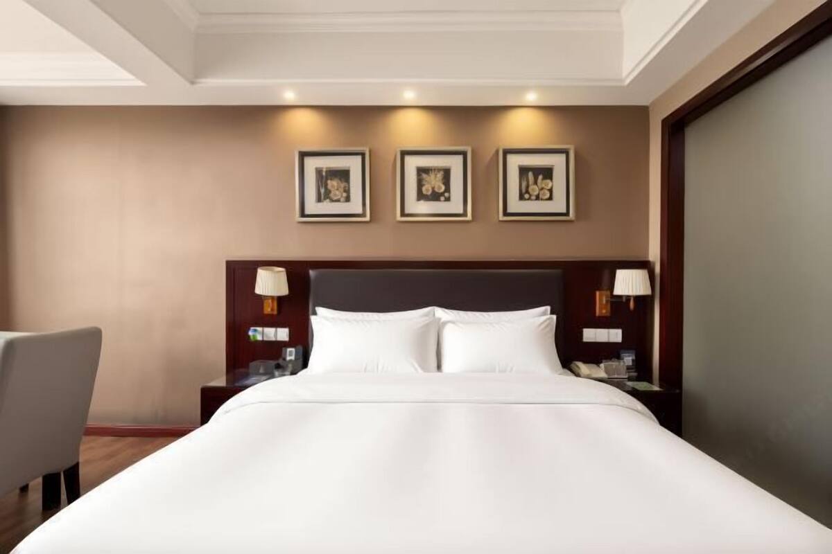 Quarto de hotel com uma cama grande, duas mesas de cabeceira com abajures, uma cadeira e três quadros na parede.