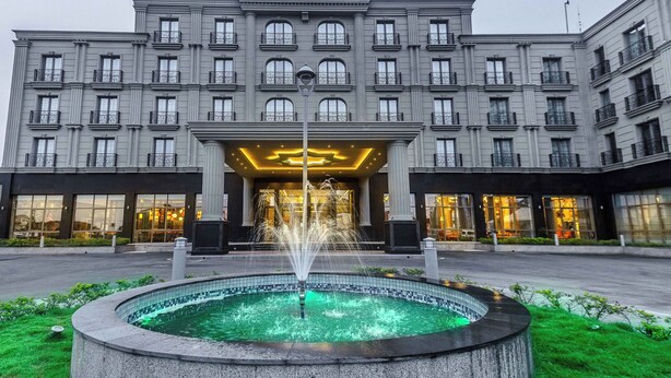 Um hotel grande, com vários andares, uma fonte central e um pátio bem cuidado.