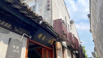 Uma rua estreita com arquitetura tradicional, incluindo um edifício com toldo preto e uma placa com caracteres chineses.