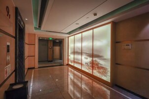 Corredor de hotel com piso lustroso, área de recepção e painel decorativo na parede.