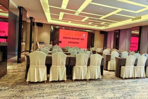 Uma sala de conferências com fileiras de mesas e cadeiras, uma tela de projeção e um palco.