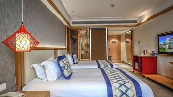 Quarto de hotel com uma cama grande, uma escrivaninha com telefone, um candeeiro pendente vermelho e uma televisão na parede.