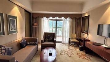 Quarto de hotel moderno com sofá, poltrona, mesa de centro redonda e uma TV.