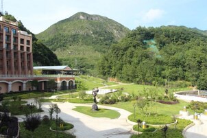 Pátio de hotel com uma escultura central, cercado por vegetação e com montanhas ao fundo.