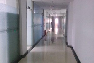 Um corredor com divisórias de vidro, uma pessoa caminhando e uma porta no final.