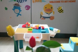 Espaço infantil com mesa, brinquedos e parede com personagens de desenho animado.