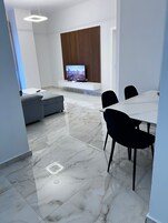 Uma sala de estar moderna com uma televisão de tela plana, um sofá e um espaço de jantar com cadeiras e uma mesa.
