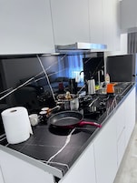 Uma cozinha moderna com bancada preta, eletrodomésticos de aço inoxidável e vista para a sala de estar através de uma janela.