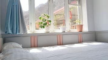 Quarto com cama, janela com cortinas e plantas em vasos no parapeito.