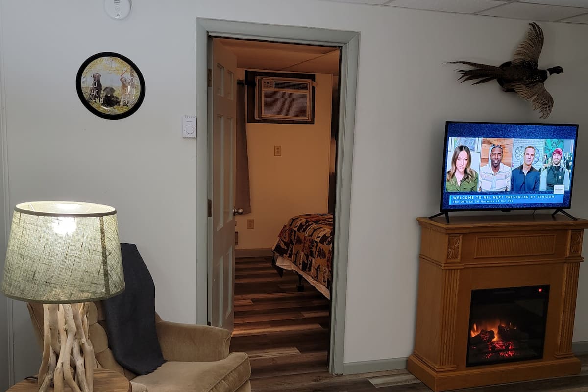 Uma sala de estar com televisão, lareira, abajur, sofá e escada que dá para outro cômodo.
