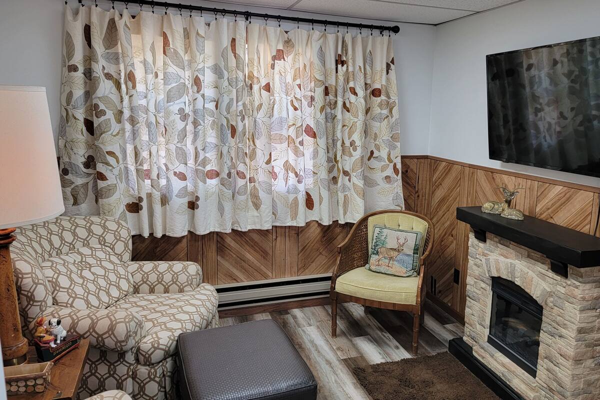 Uma sala de estar com lareira, televisão na parede e sofá estampado.