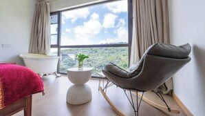 Quarto moderno com uma janela grande, uma banheira, uma cadeira de balanço e um cobertor vermelho.