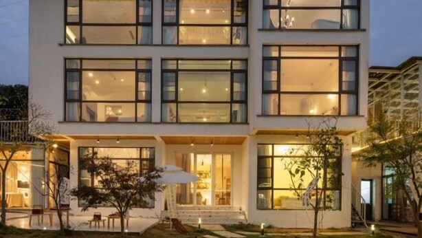 Um edifício moderno de dois andares, com grandes janelas, entrada coberta e uma pequena área de estar ao ar livre.