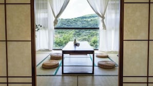 Quarto com tatames, uma mesa baixa e vista para uma paisagem verde através de cortinas translúcidas.
