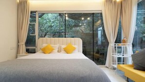 Quarto com cama grande, cortinas bege e vista para o verde lá fora.
