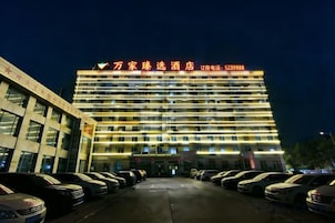 Hotel de vários andares com uma fileira de janelas iluminadas e um estacionamento na frente.
