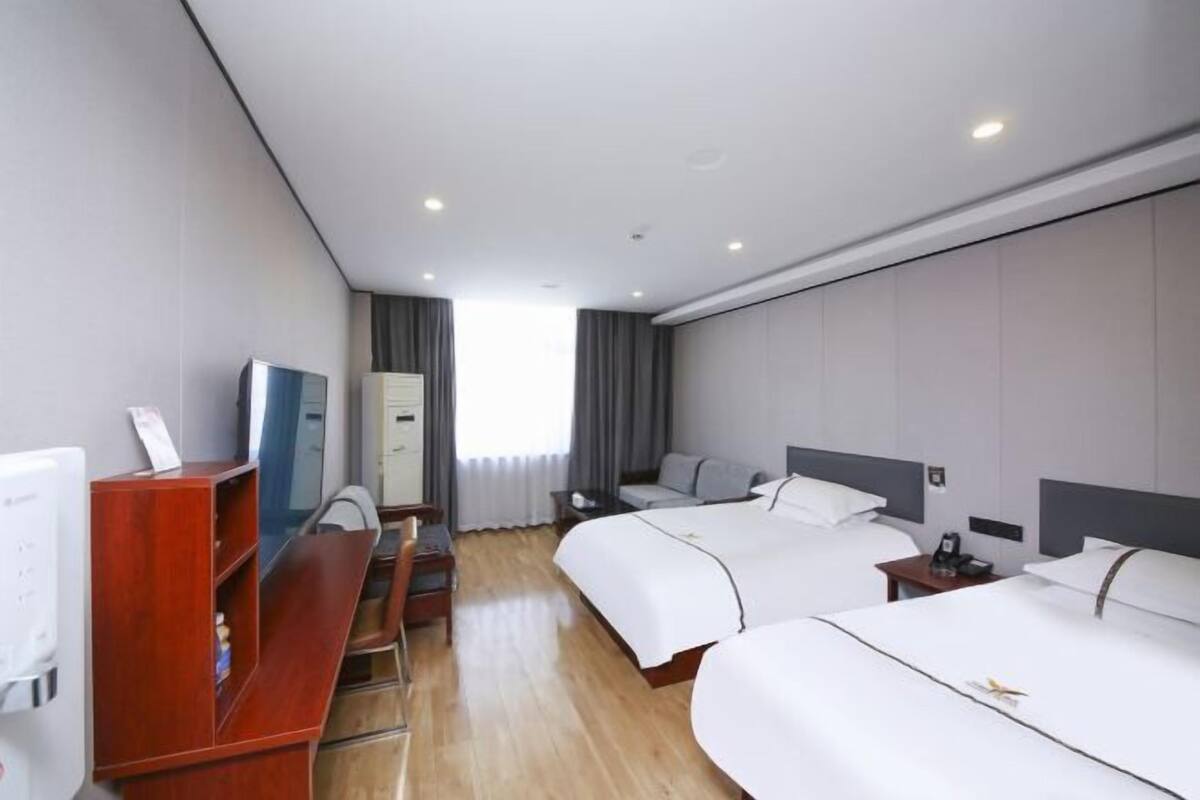 Quarto de hotel com duas camas, uma escrivaninha, televisão e guarda-roupa.