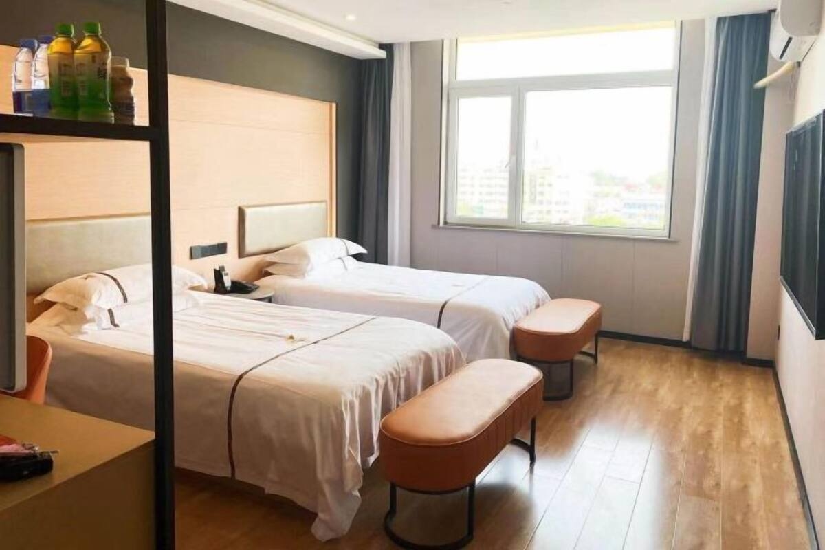 Quarto de hotel com duas camas, um banco, uma escrivaninha e uma janela com vista.