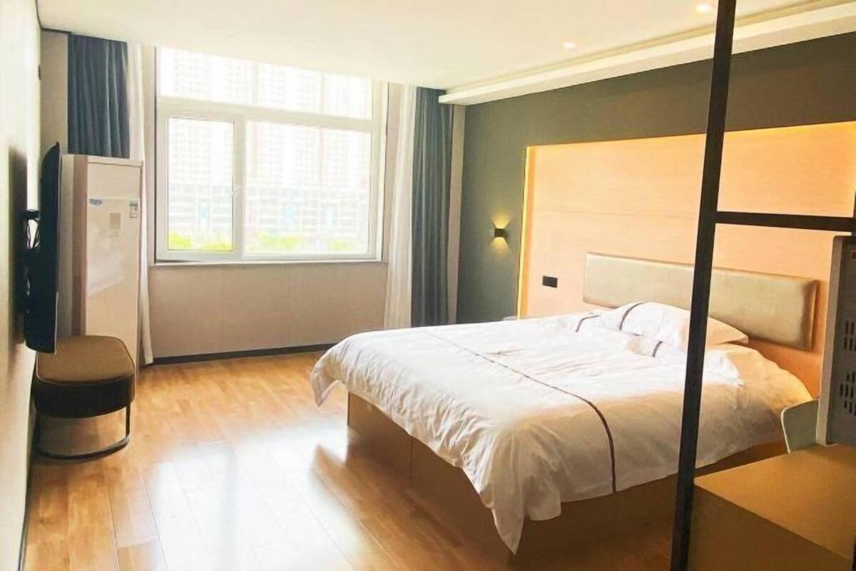 Quarto de hotel com cama, televisão, janela e piso de madeira.