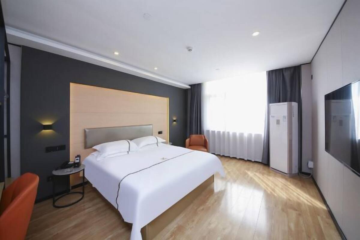 Quarto de hotel moderno com uma cama grande, uma escrivaninha, uma cadeira, uma televisão e uma janela com cortinas.