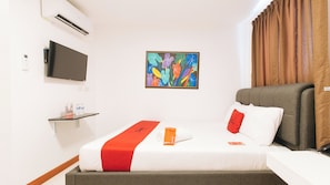 Quarto de hotel com uma cama, televisão, um quadro, uma prateleira com artigos de higiene e uma janela com cortinas.
