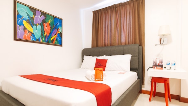 Quarto de hotel com cama, escrivaninha, cadeira, pintura e janela com cortinas.