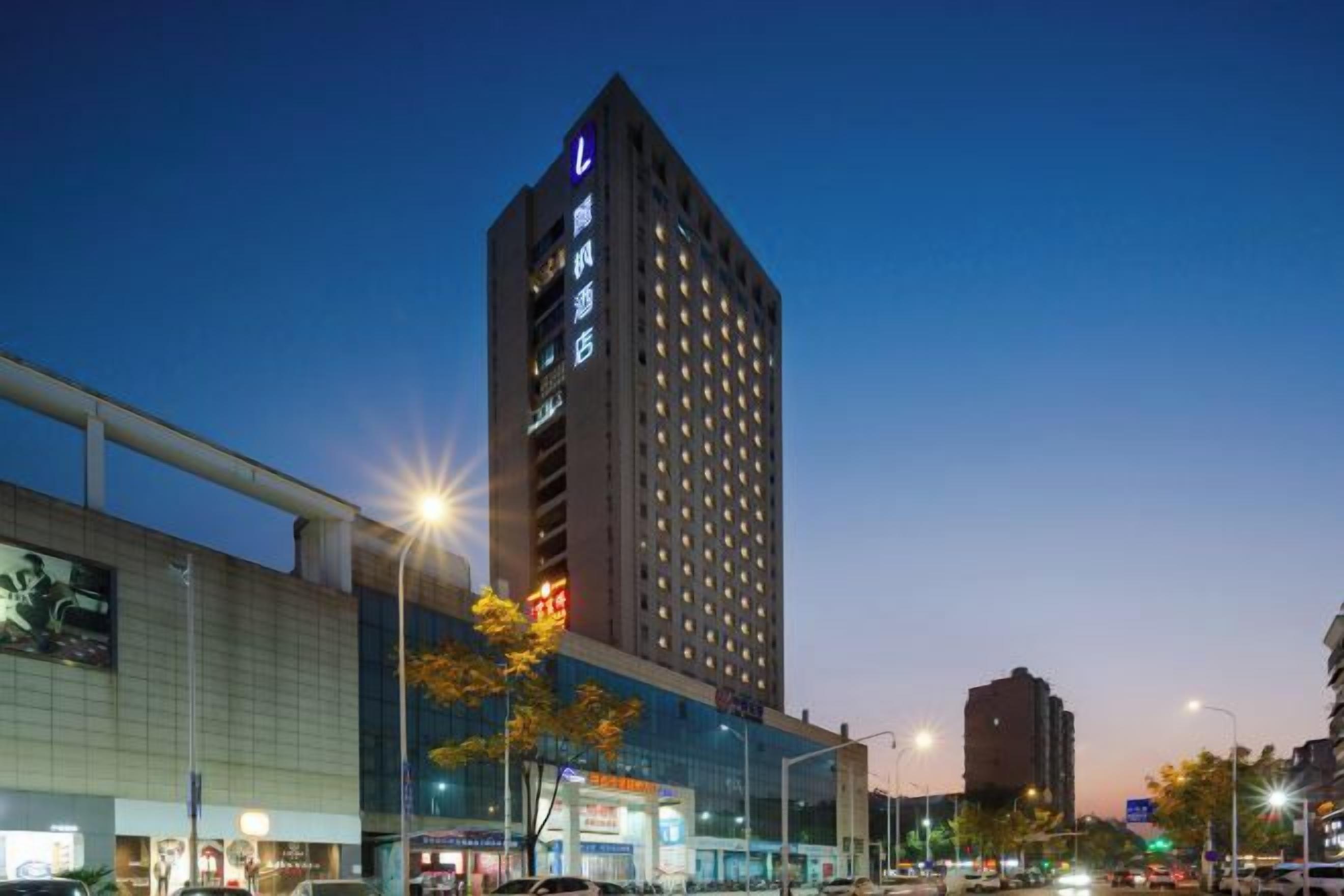 Um hotel moderno com um logotipo 'L' bem visível, rodeado por uma movimentada rua urbana ao entardecer.